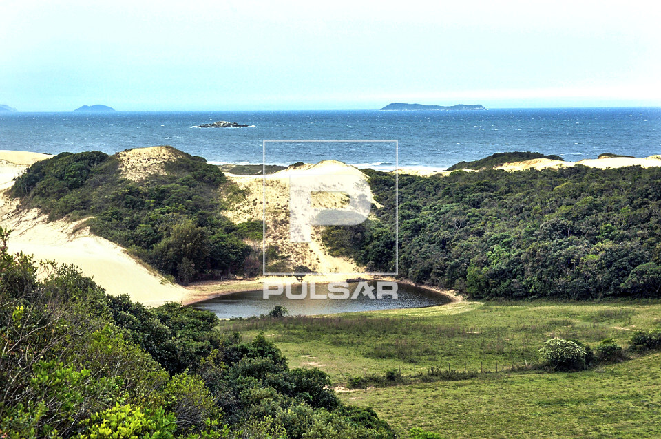 Lagoa em meio as dunas e vegetação com mar ao fundo na Praia do Siriu ...