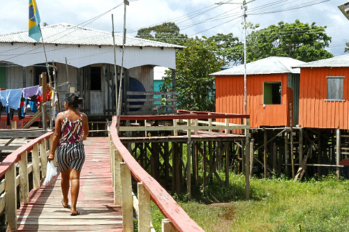 Ribeirinha caminhando em passarela de madeira de acesso às palafitas na ...